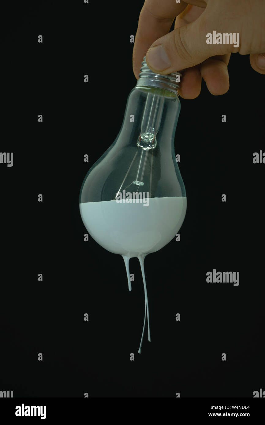 Hand holding big light bulb with dripping white paint on a black ...