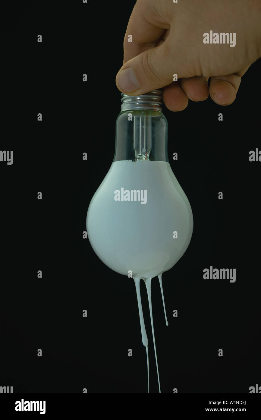 Hand holding big light bulb with dripping white paint on a black ...