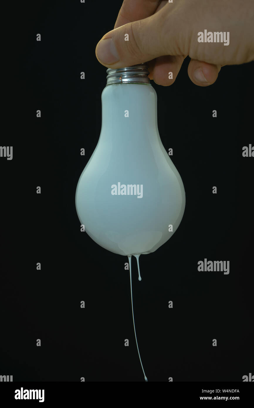 Hand holding big light bulb with dripping white paint on a black ...