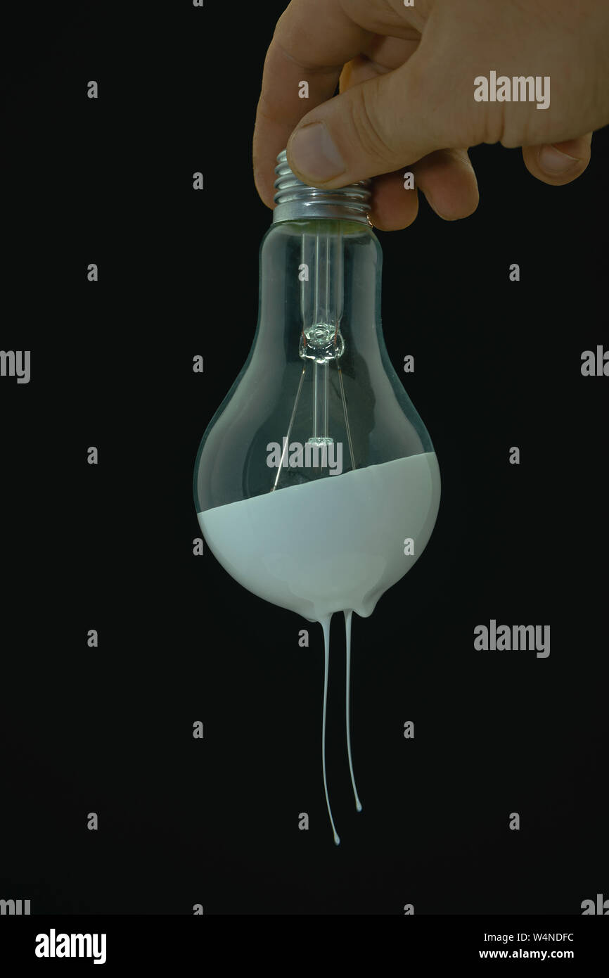 Hand holding big light bulb with dripping white paint on a black ...