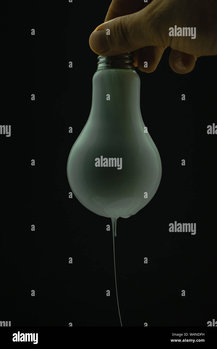 Hand holding big light bulb with dripping white paint on a black ...