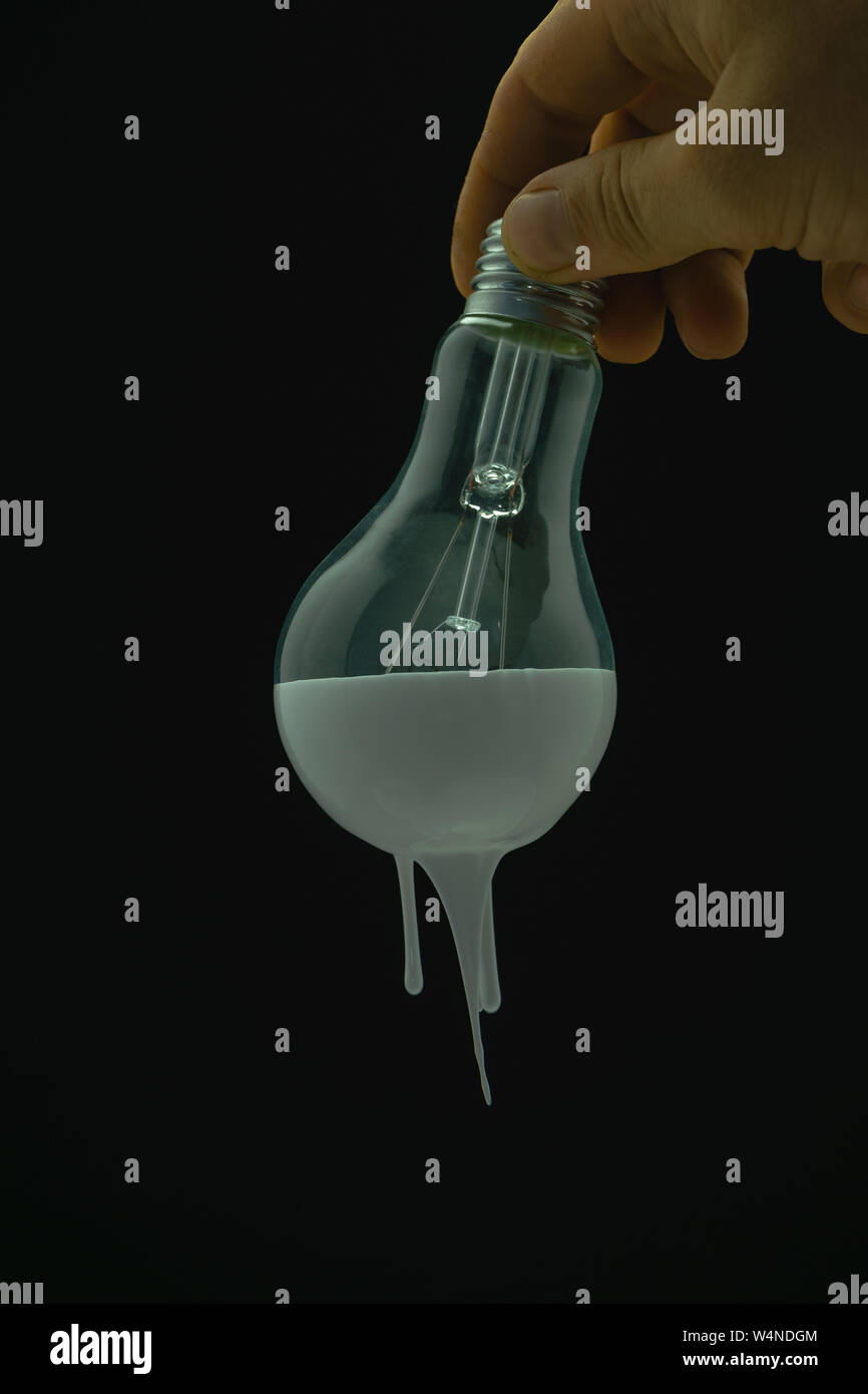 Hand holding big light bulb with dripping white paint on a black ...