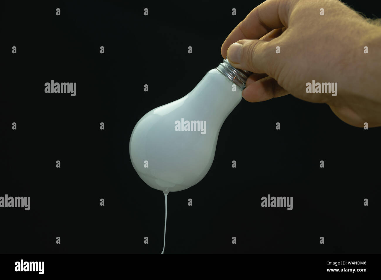 Hand holding big light bulb with dripping white paint on a black ...