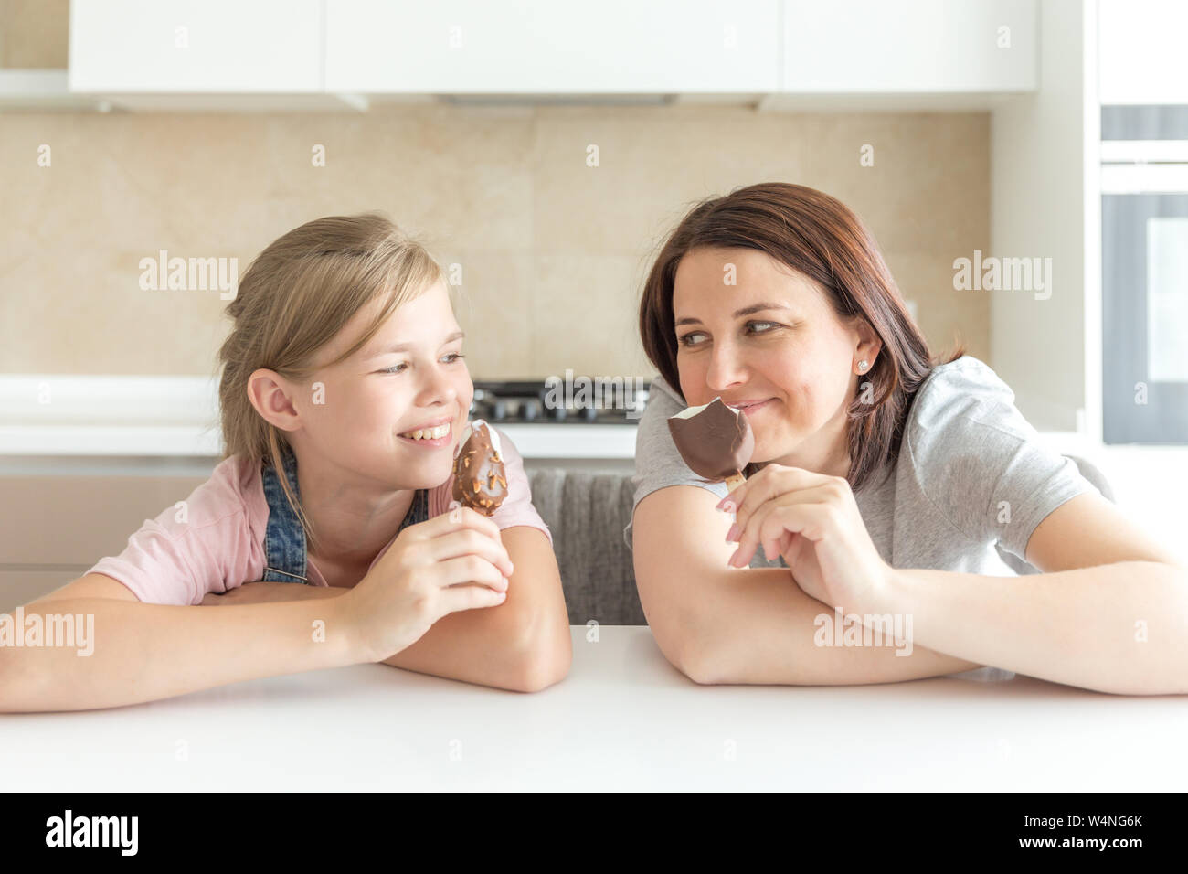 Mother with her 12 years old daughter sitting in the kitchen eating ice ...