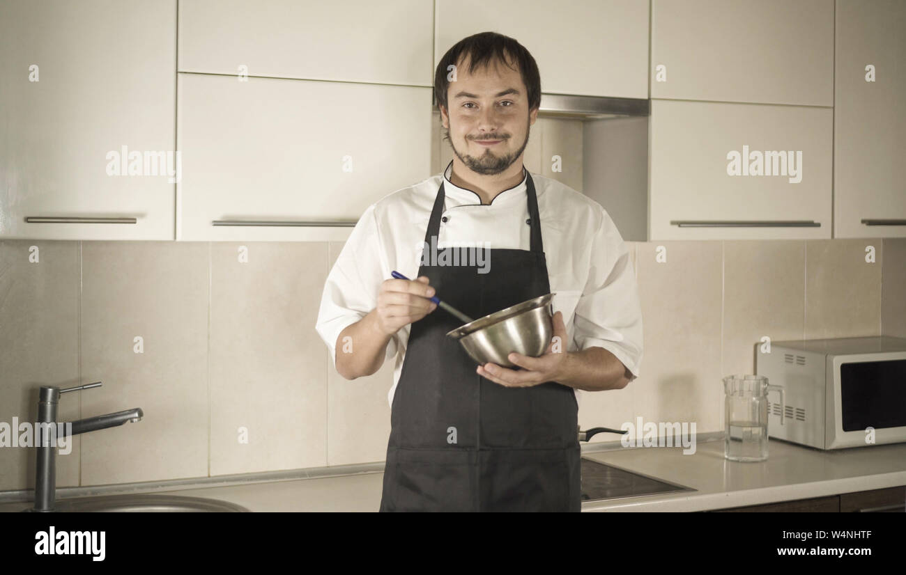 Attractive young funny man dancing while cooking in the kitchen at home ...