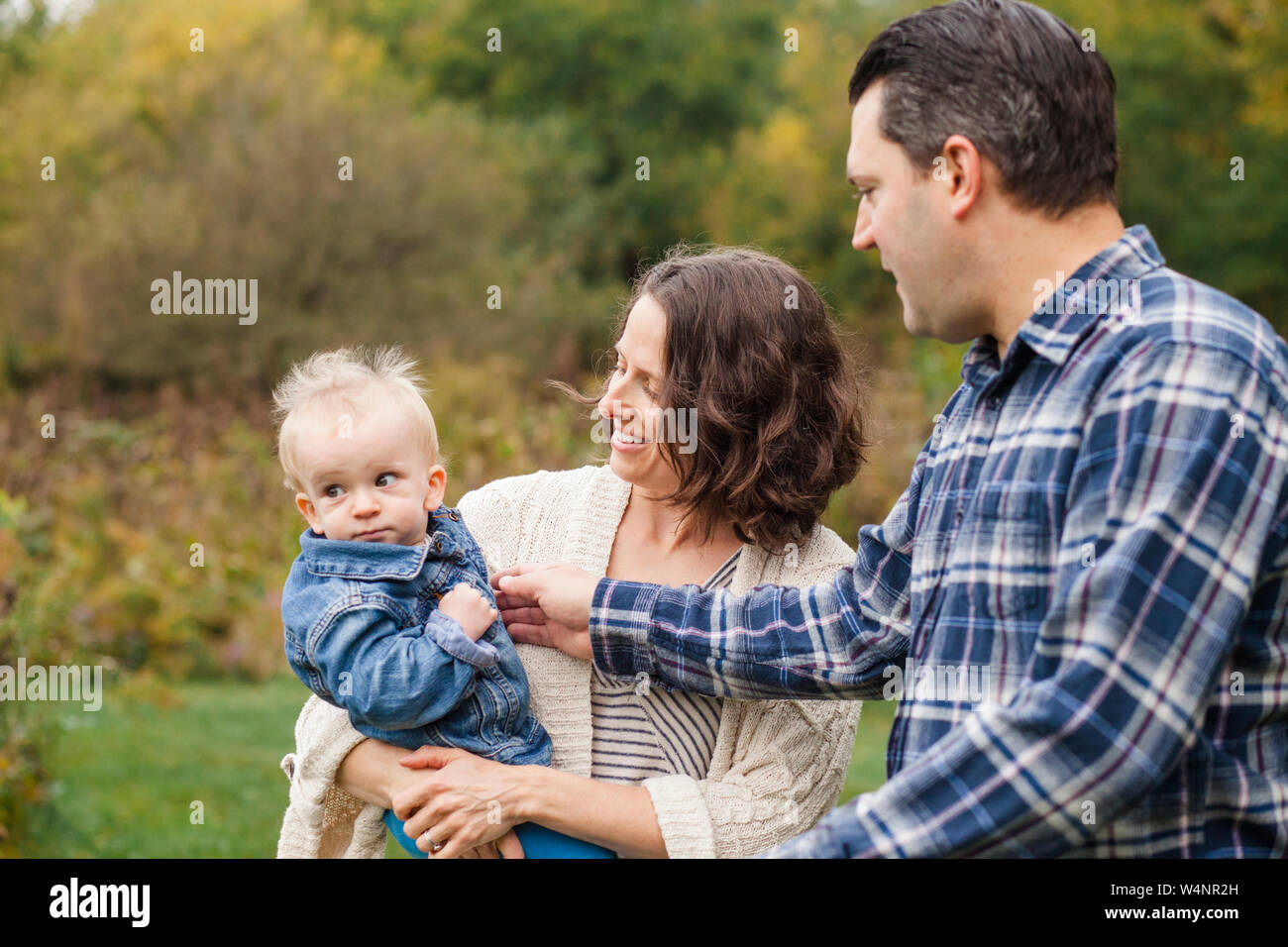 a smiling mother and father talk a walk with their small toddler son ...
