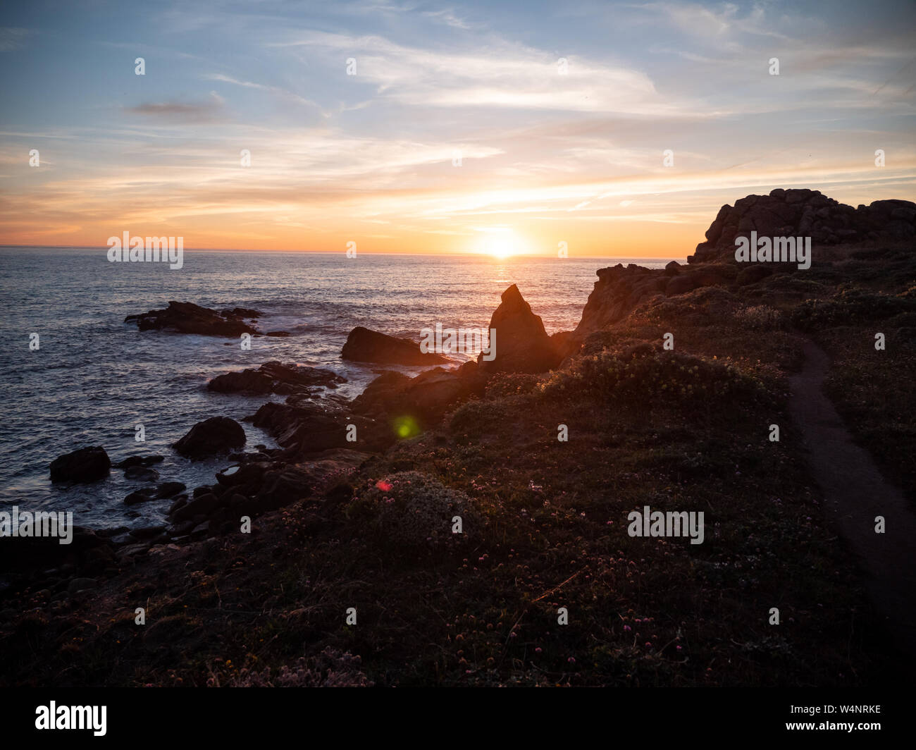 Sun setting over ocean with rugged coastline Stock Photo - Alamy
