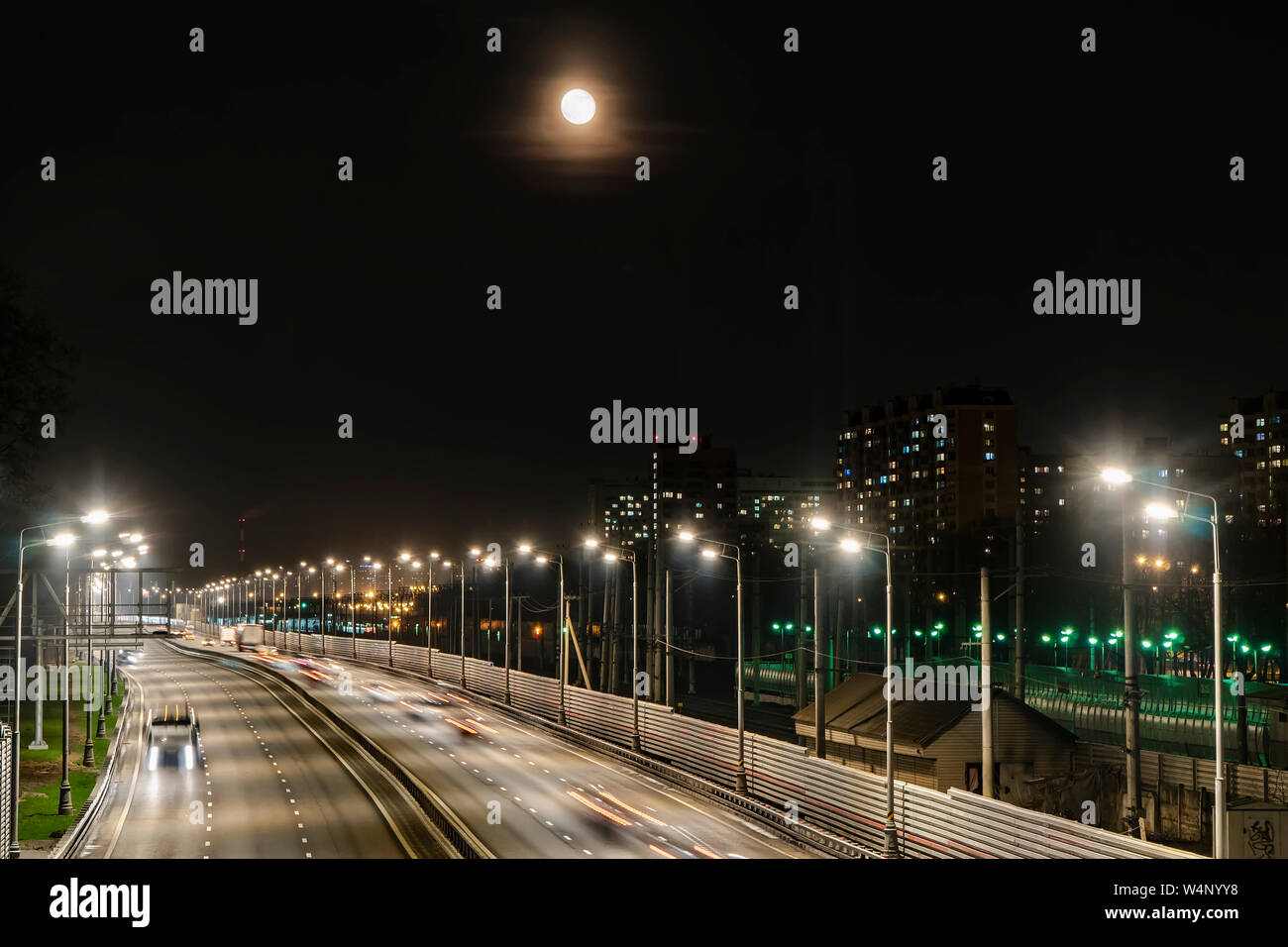 The moon rising over the illuminated highway and the night city Stock ...