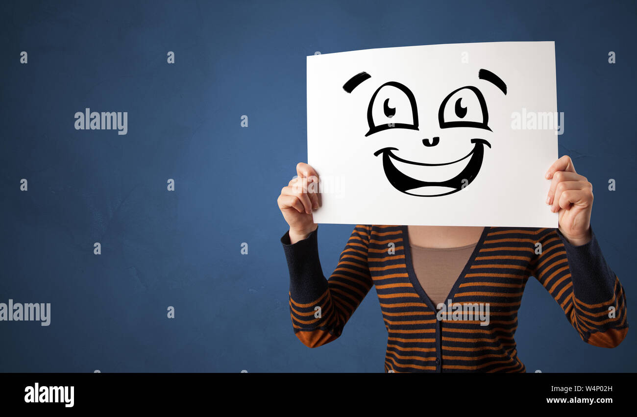 Casual person holding a paper in front of his face with drawn emoticon ...