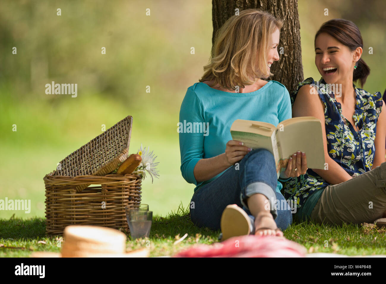 Happy friends reading a book together under a tree at the park Stock ...
