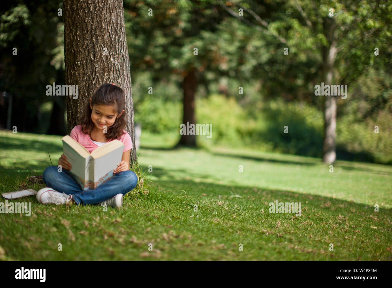 Happy young girl reading a book under a tree Stock Photo - Alamy