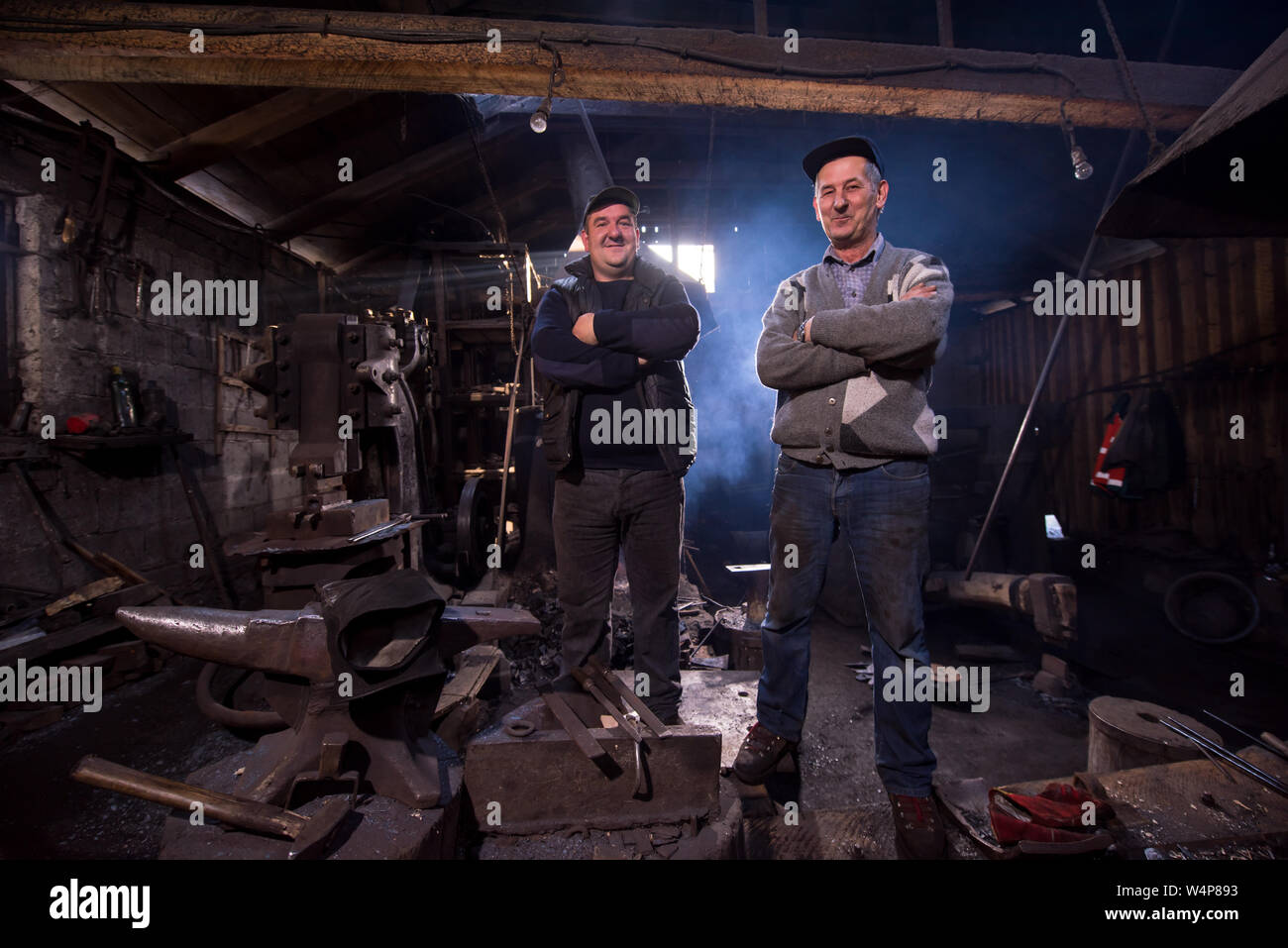 portrait of two generations confident blacksmith standing with crossed ...