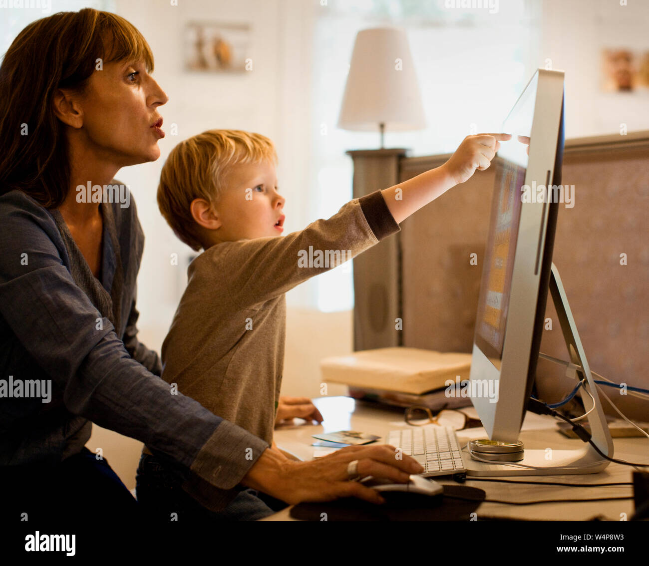Young boy sitting with his mother at a home study desk points at a ...