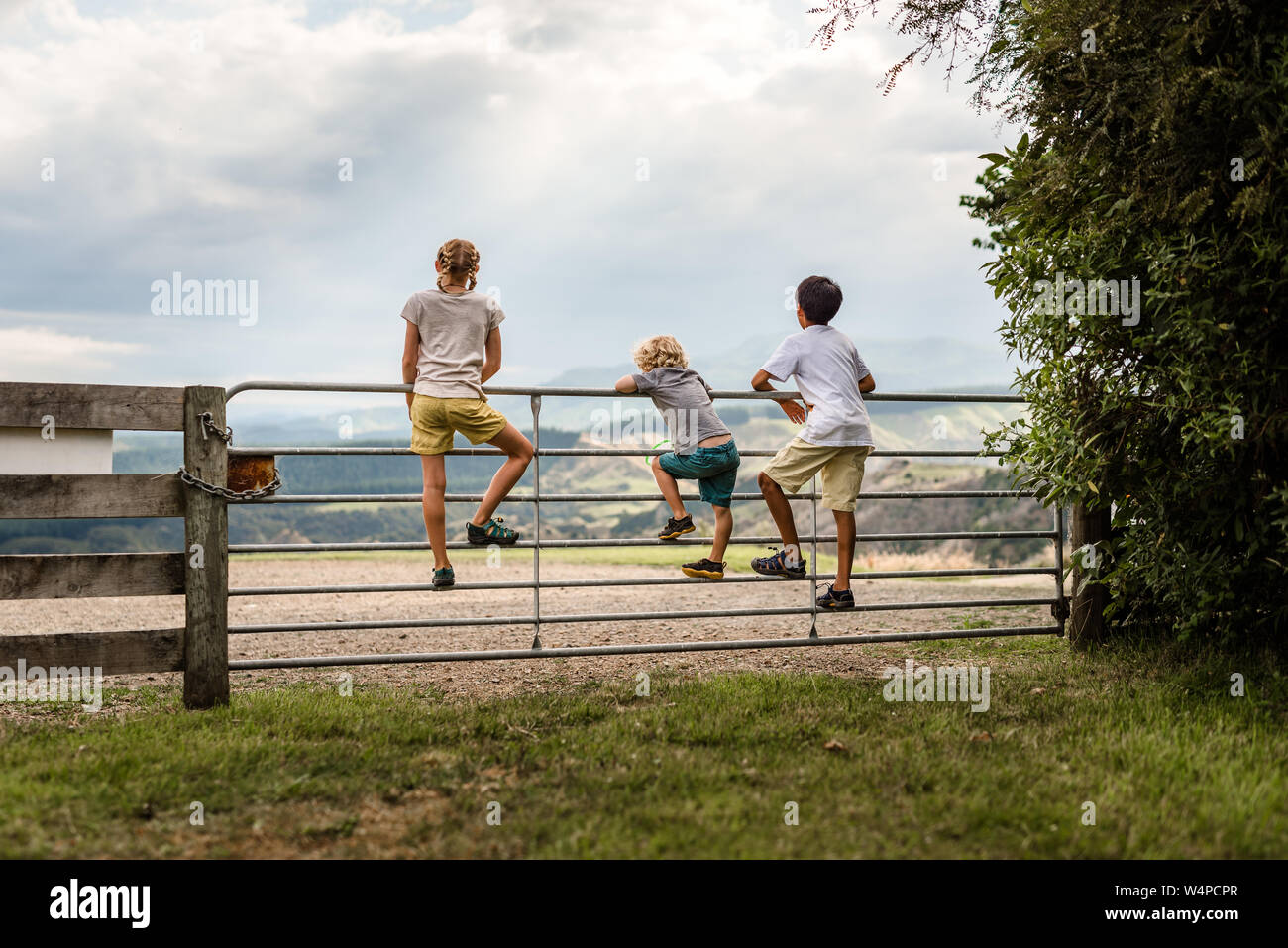 Three kids climbing on a gate with mountains in the distance Stock ...