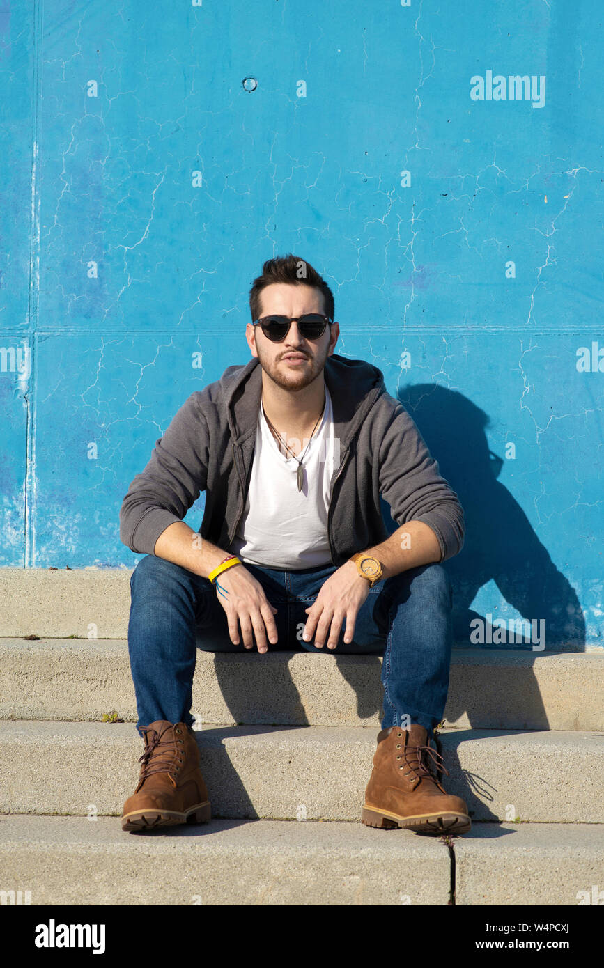 Front view of young bearded man sitting on outdoors staircase, looking ...