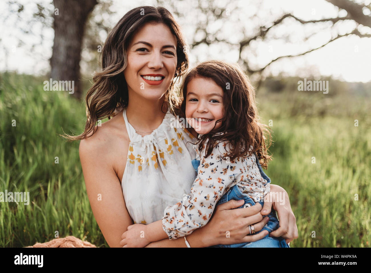 Portrait of mother and daughter in backlit field smiling at camera ...