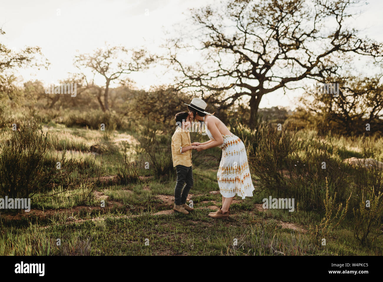 Young mother bending down to kiss young son in backlit meadow Stock ...