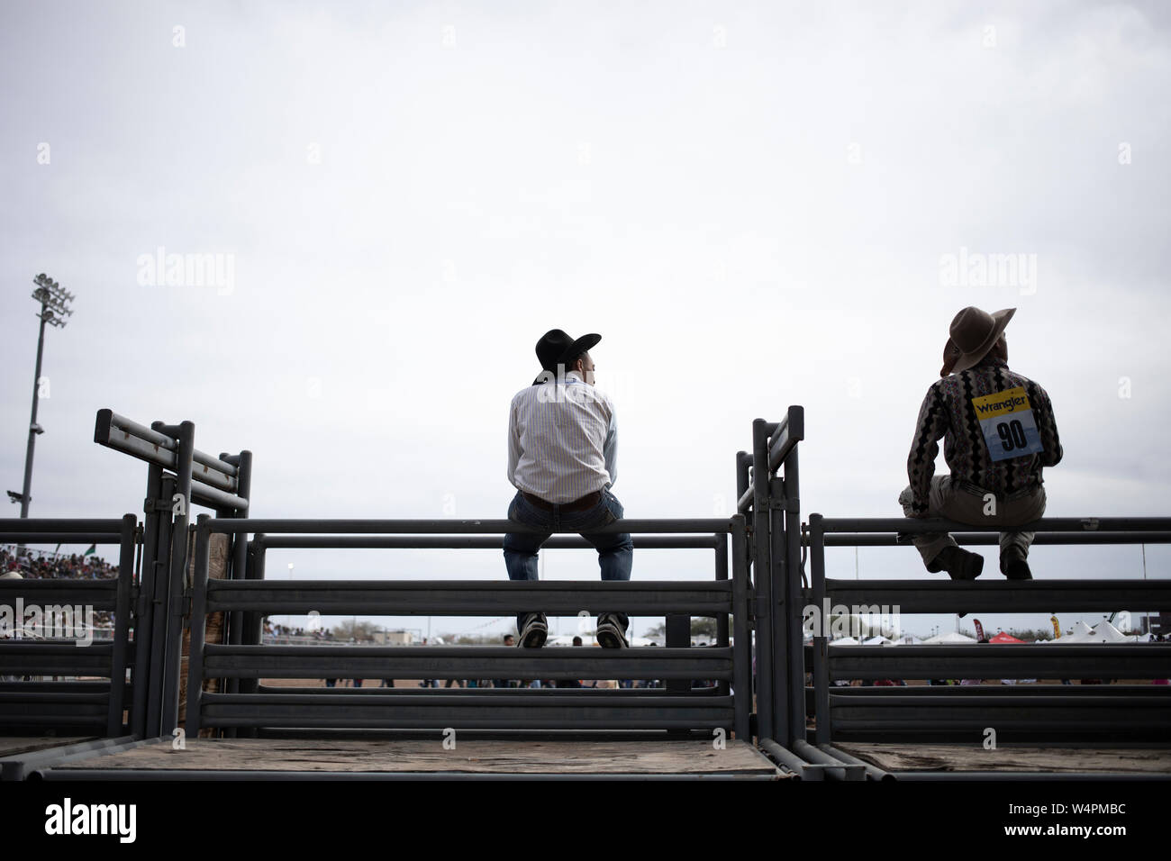 Nearly silhouetted cowboys sit on a fence at the Arizona Black Rodeo ...
