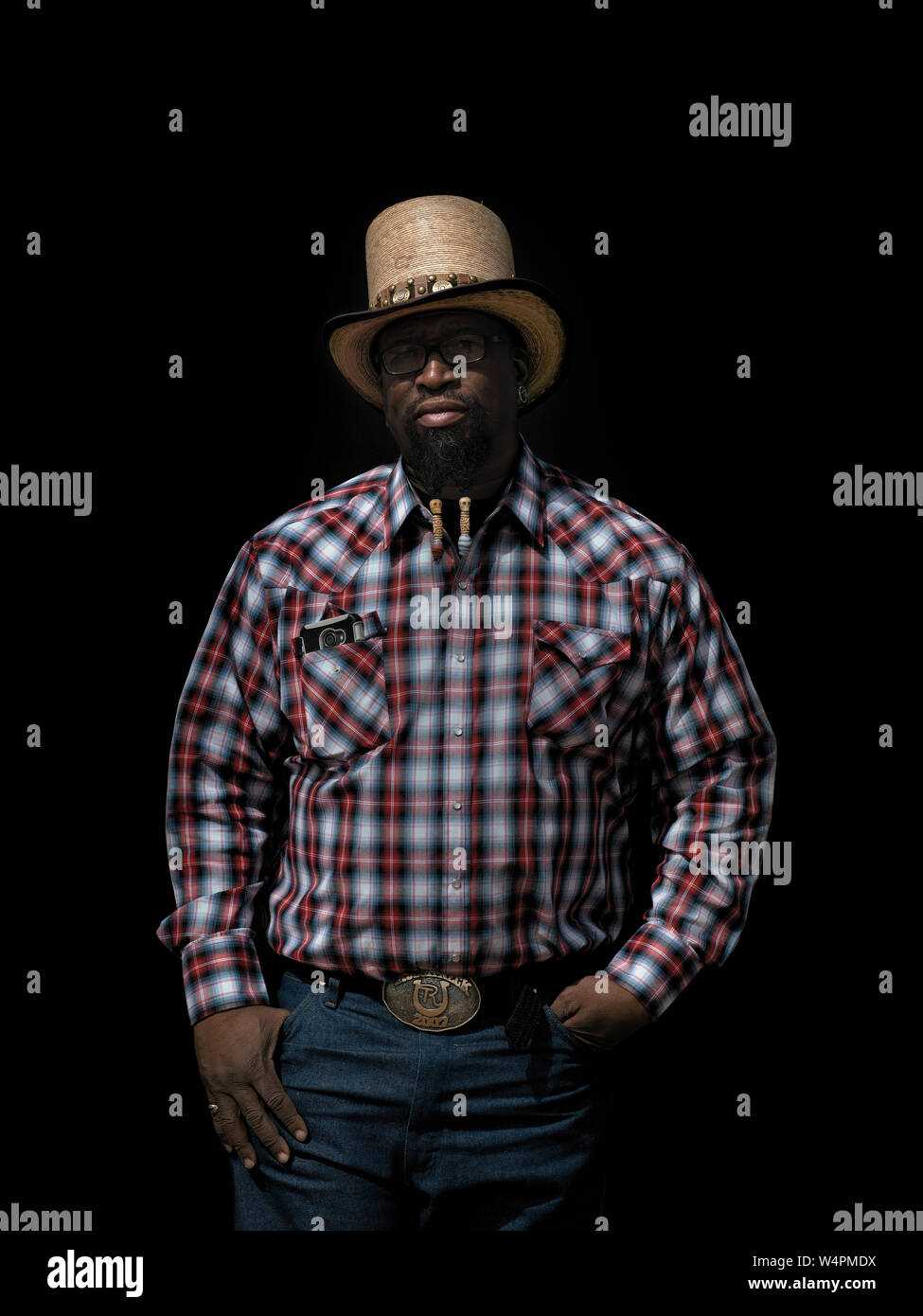 A cowboy poses for a portrait against black in available sunlight Stock ...