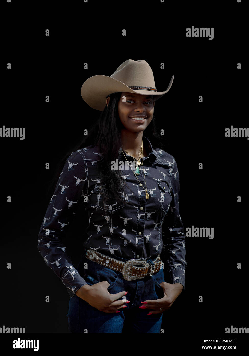 A rodeo cowgirl poses for a portrait against black in the daylight ...