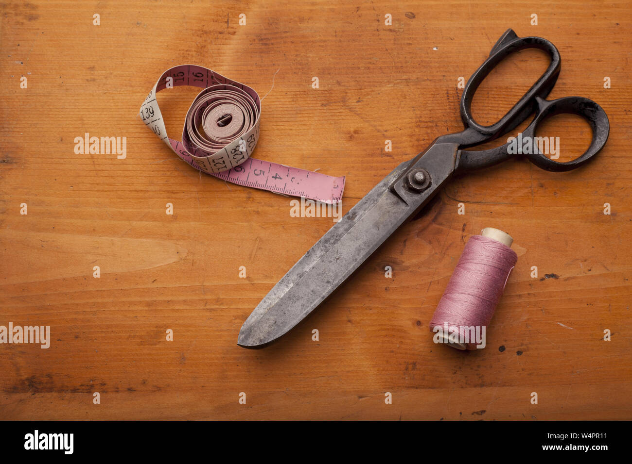 dressmaker shears craft concept with spool and measuring tape on wooden ...