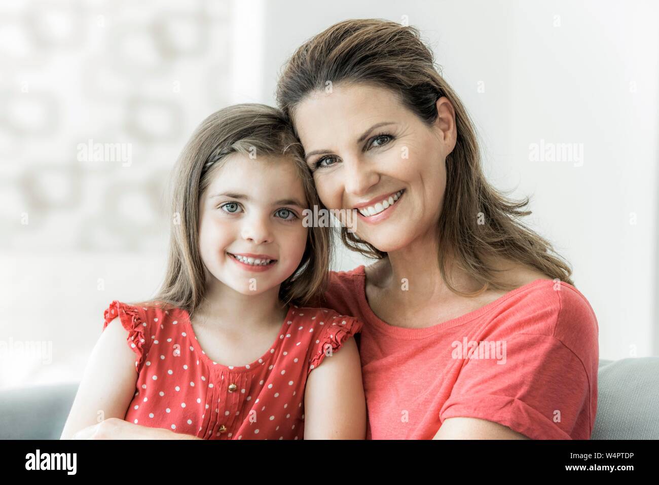 Mother and daughter sit together on the couch and look into the camera ...