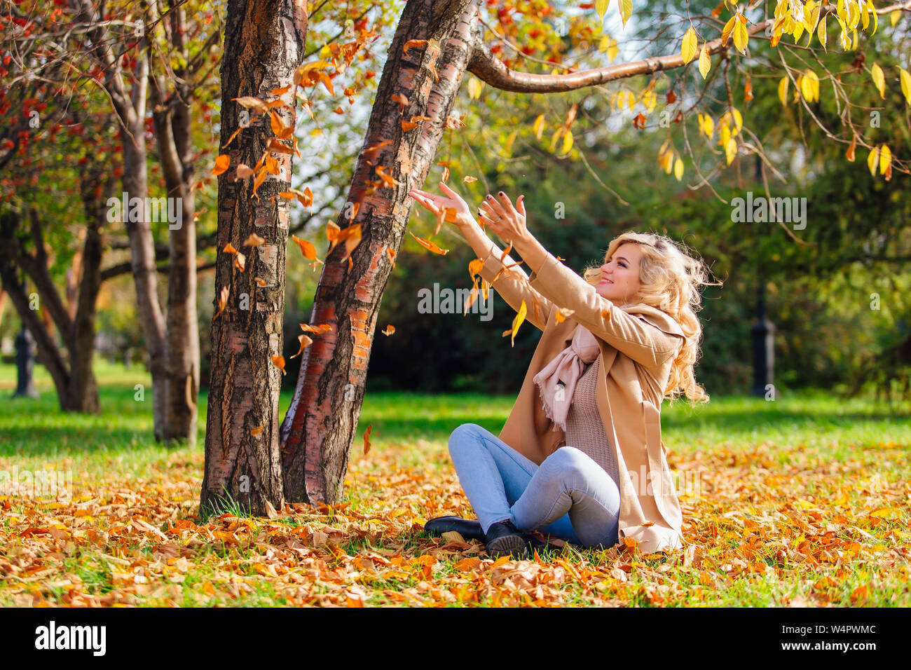 Young beautiful blonde woman throwing up fallen autumn leaves over her ...