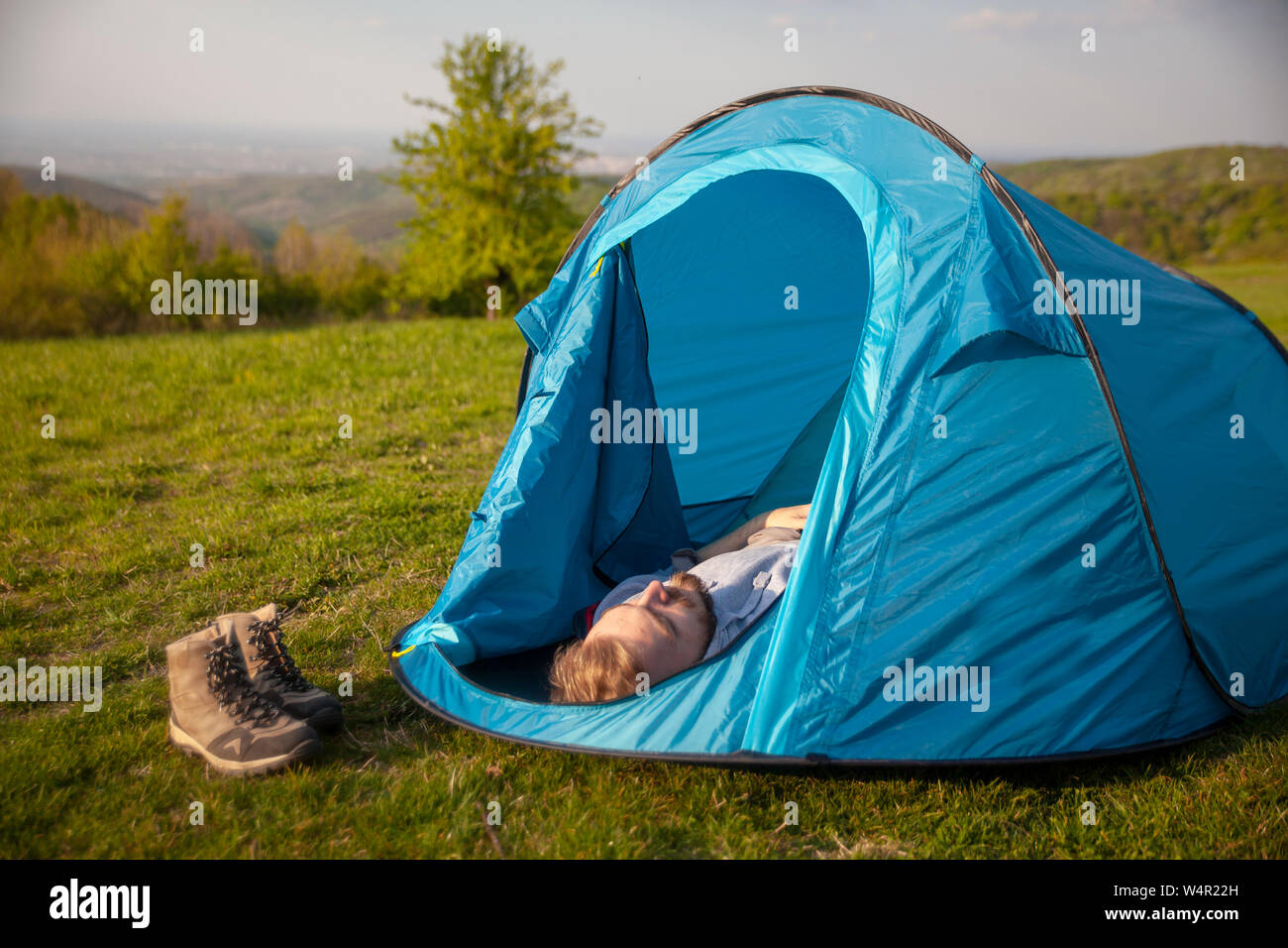 one young man, sleeping in small tent, in a grass field, in mountain ...