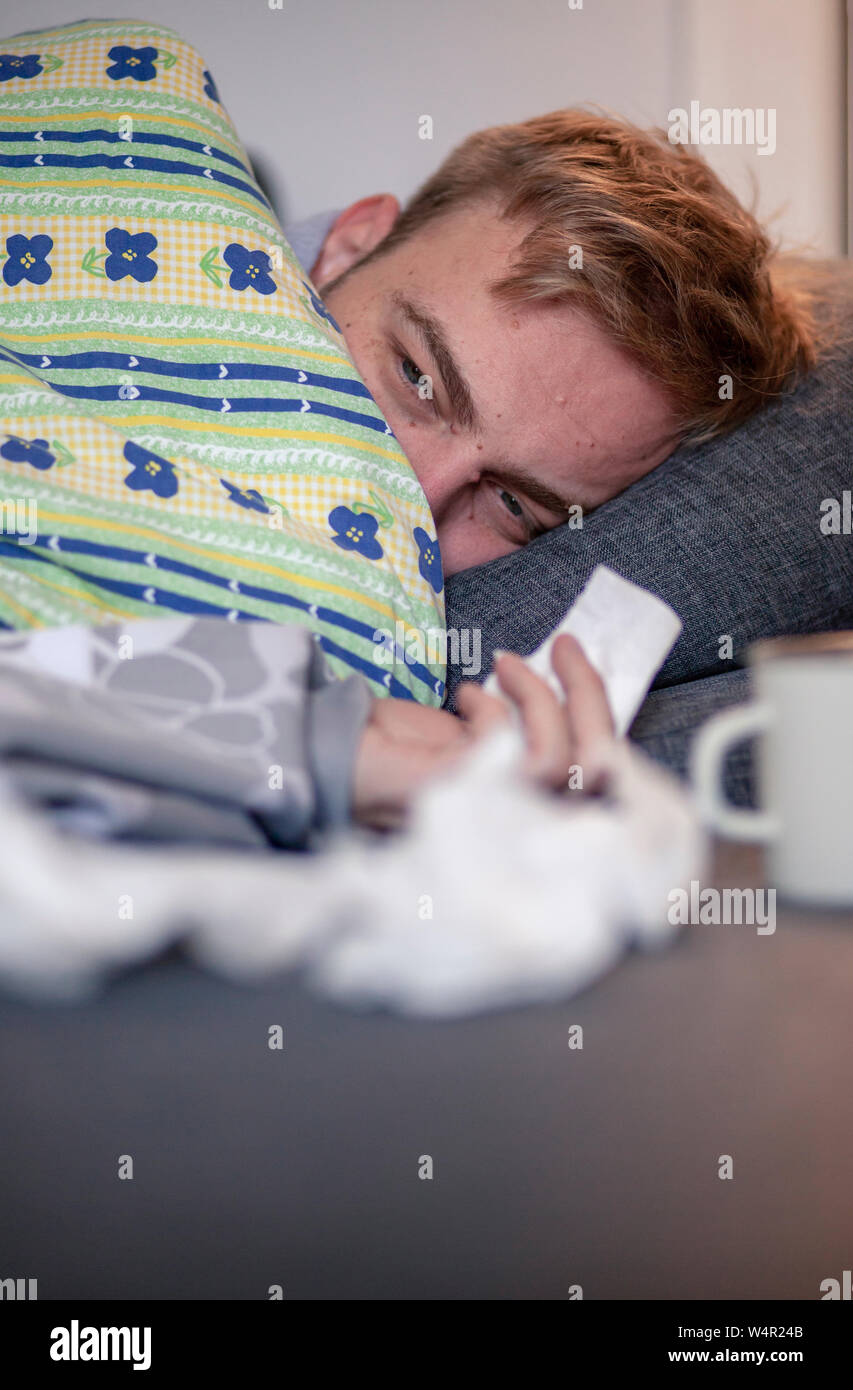 one young man, feeling sick, laying in bed, surrounded with tissue ...
