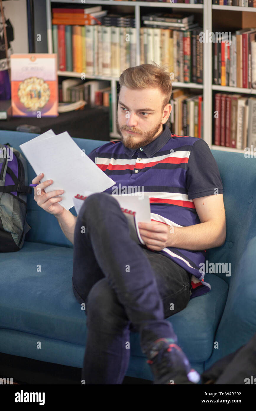 one young thoughtful man thinking, while holding papers, in a library ...