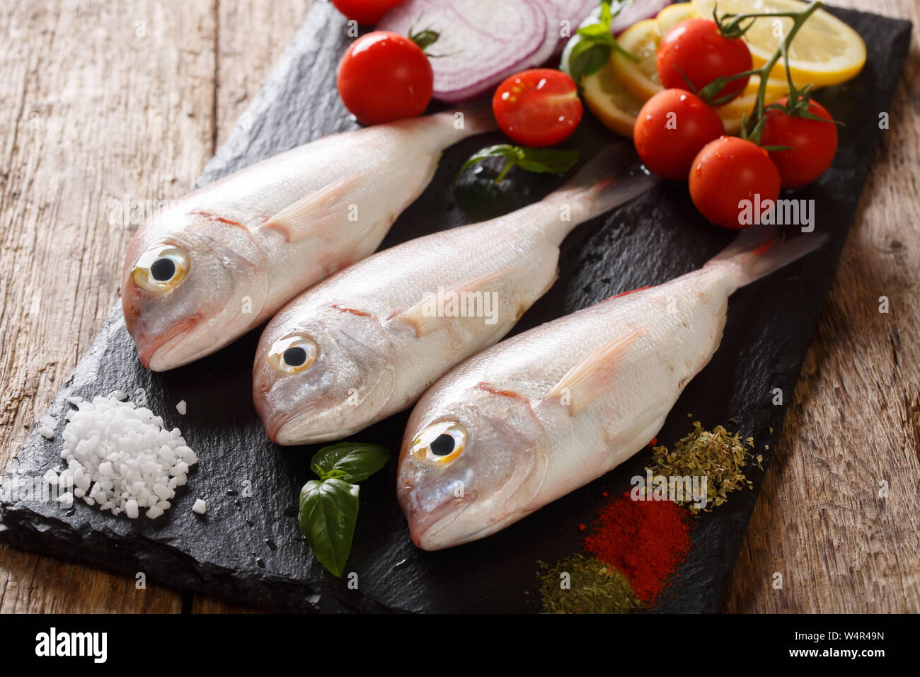 Raw pink dorado fish with spices, vegetables and lemon close-up on a ...