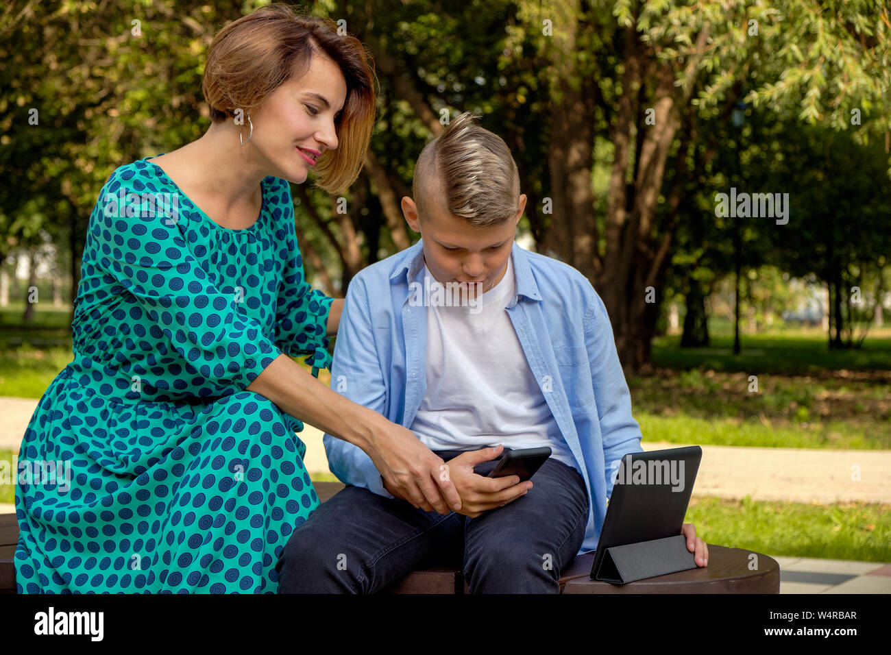 Mom and son using tablet and smartphone while sitting on nature. The ...