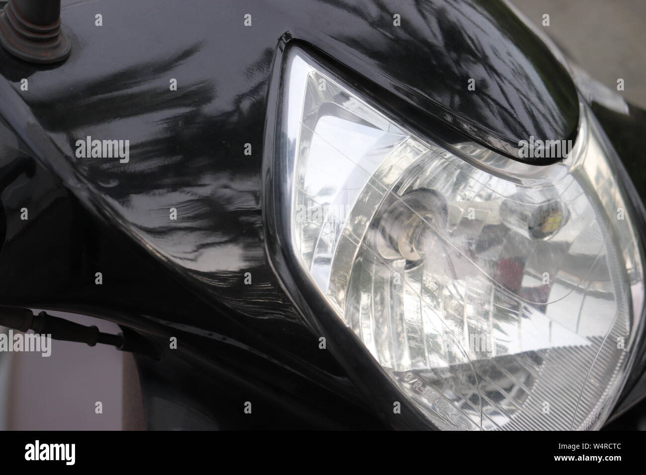 Close up of the headlamp of a black scooter resting with head tilted ...