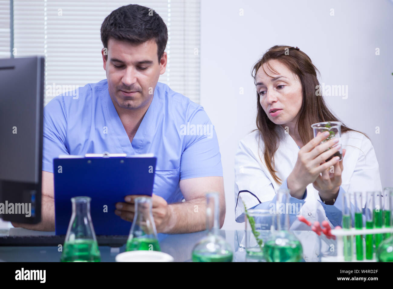 Young assistant writing notes on his notepad in a research lab. Female ...