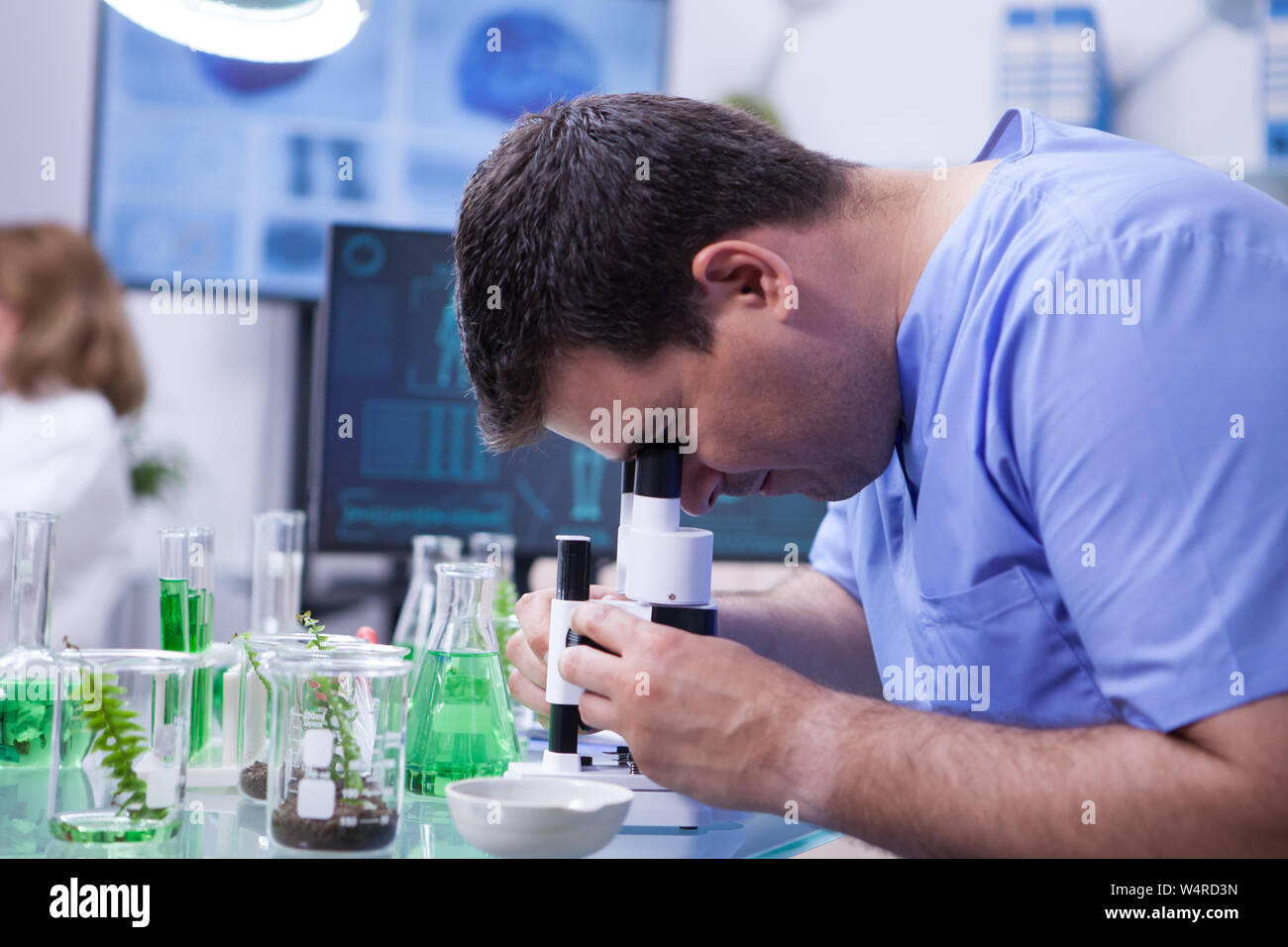 Young scientist man doing a quality control looking through microscope ...