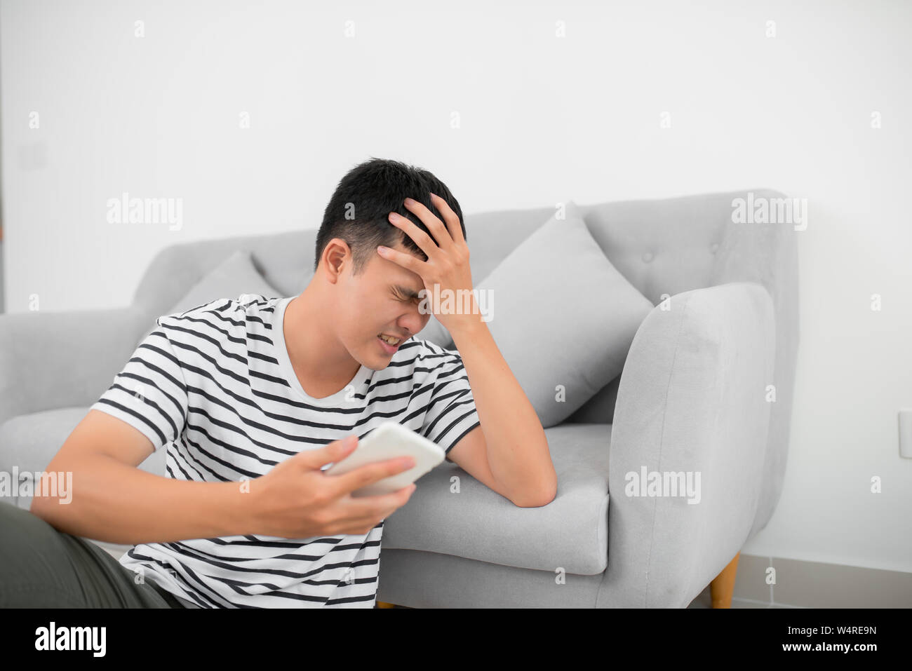 Single sad man checking mobile phone sitting on the floor in the living ...