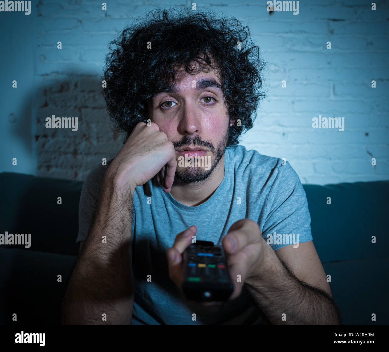 Young bored man on couch using TV remote control zapping for another ...