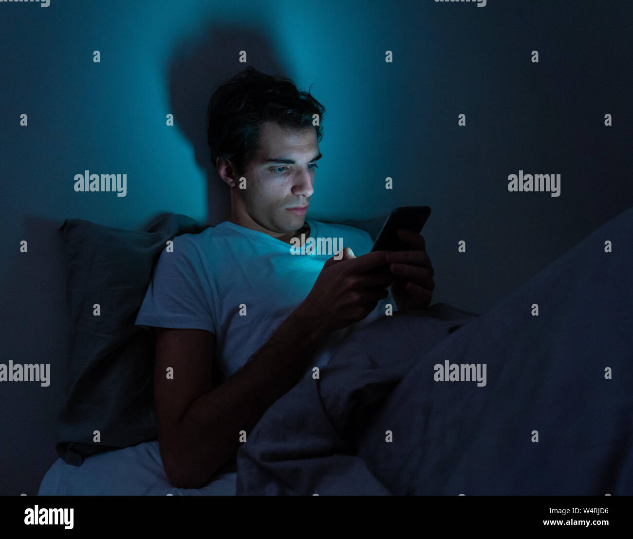 Lifestyle portrait of cell phone addict man awake late at night in bed ...