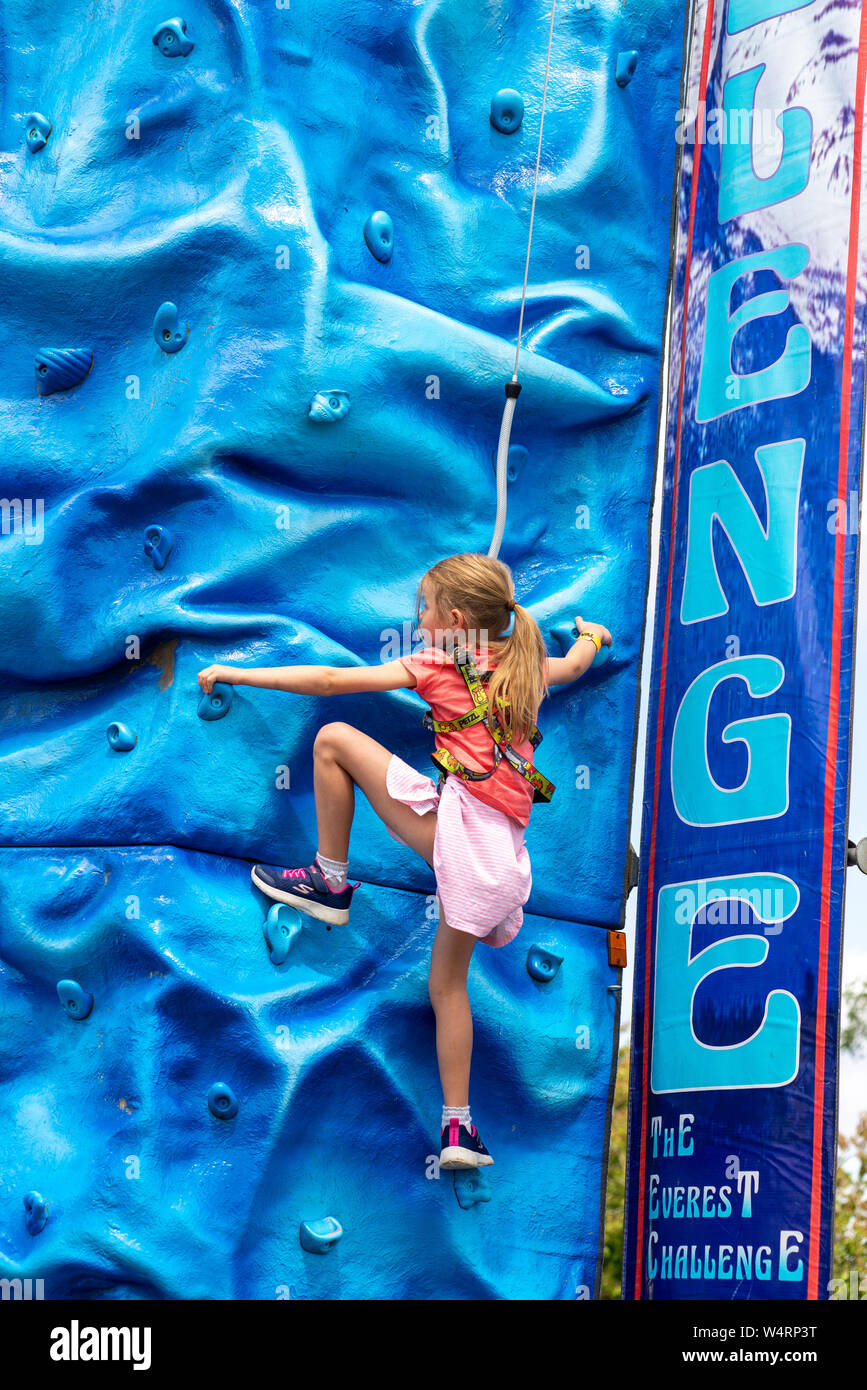Girl child ascending a climbing wall at a summer fete, England, UK ...