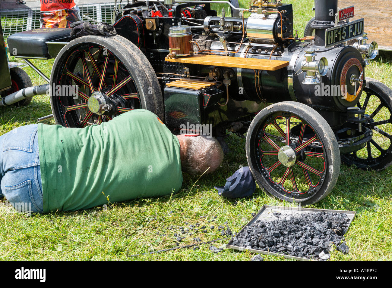 Man lying down under a steam engine to repair it at a summer fete ...