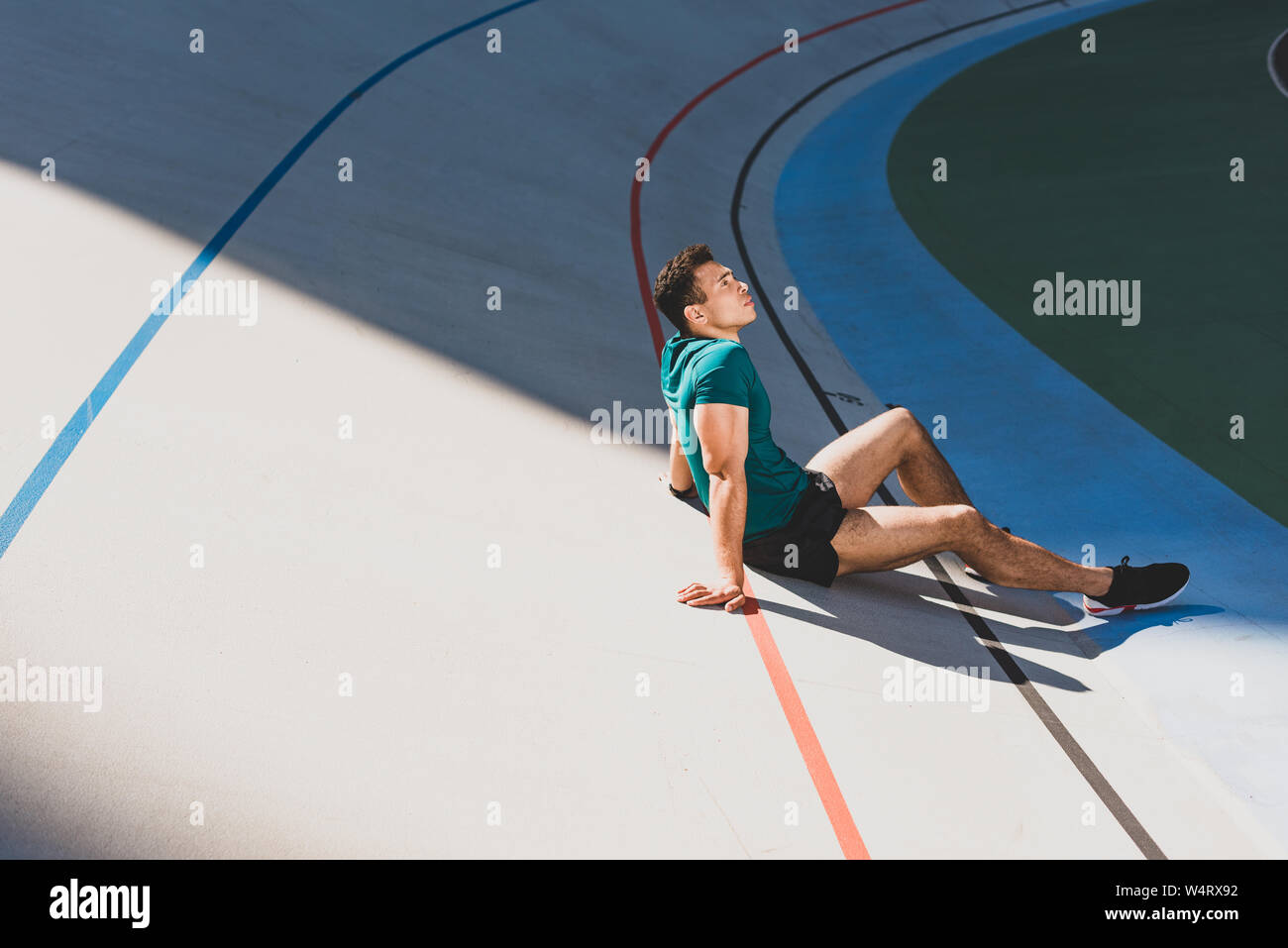 side view of mixed race sportsman sitting on running track at stadium ...