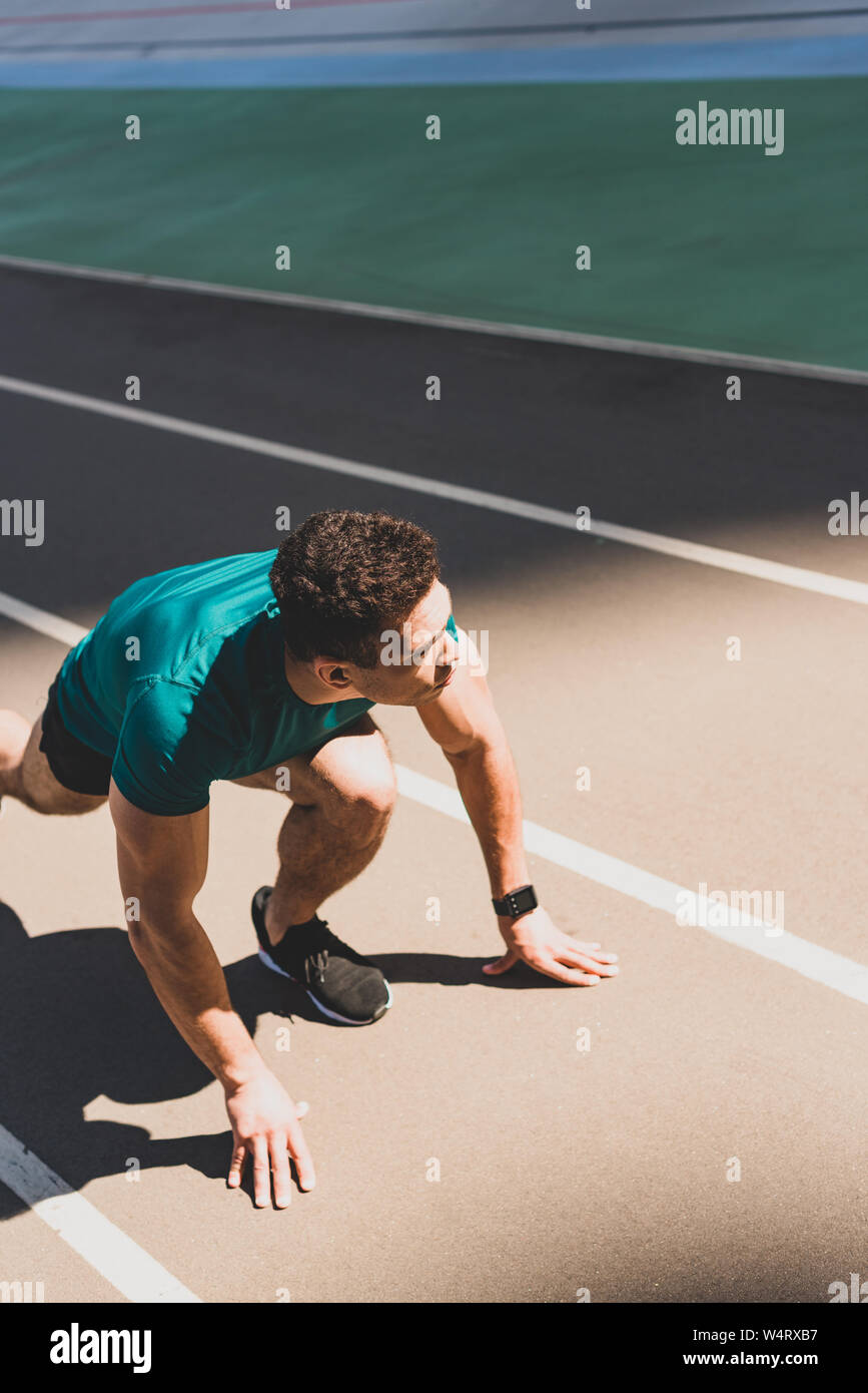 mixed race sportsman on start position on running track, looking away ...
