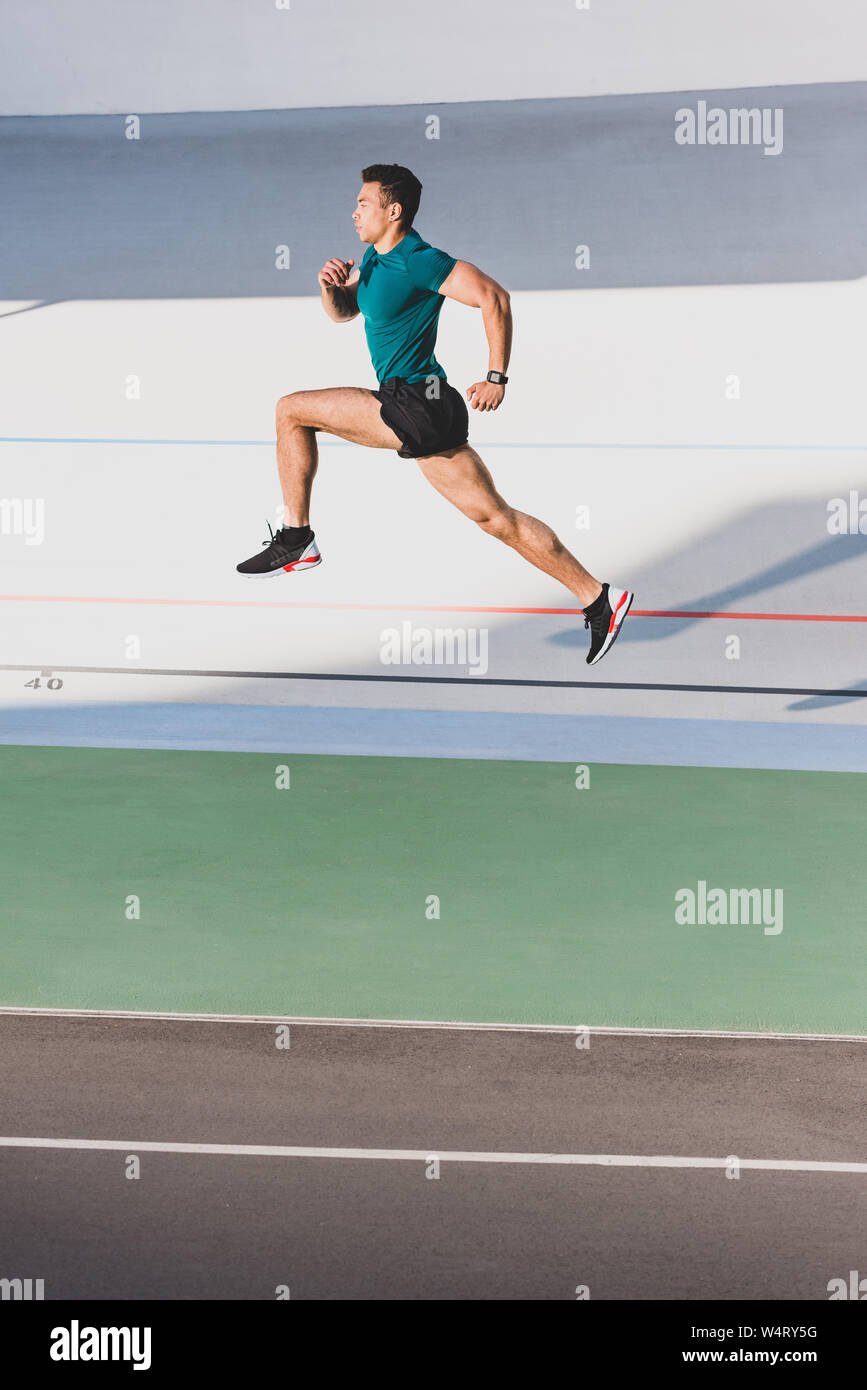 side view of muscular mixed race sportsman sprint running at stadium ...