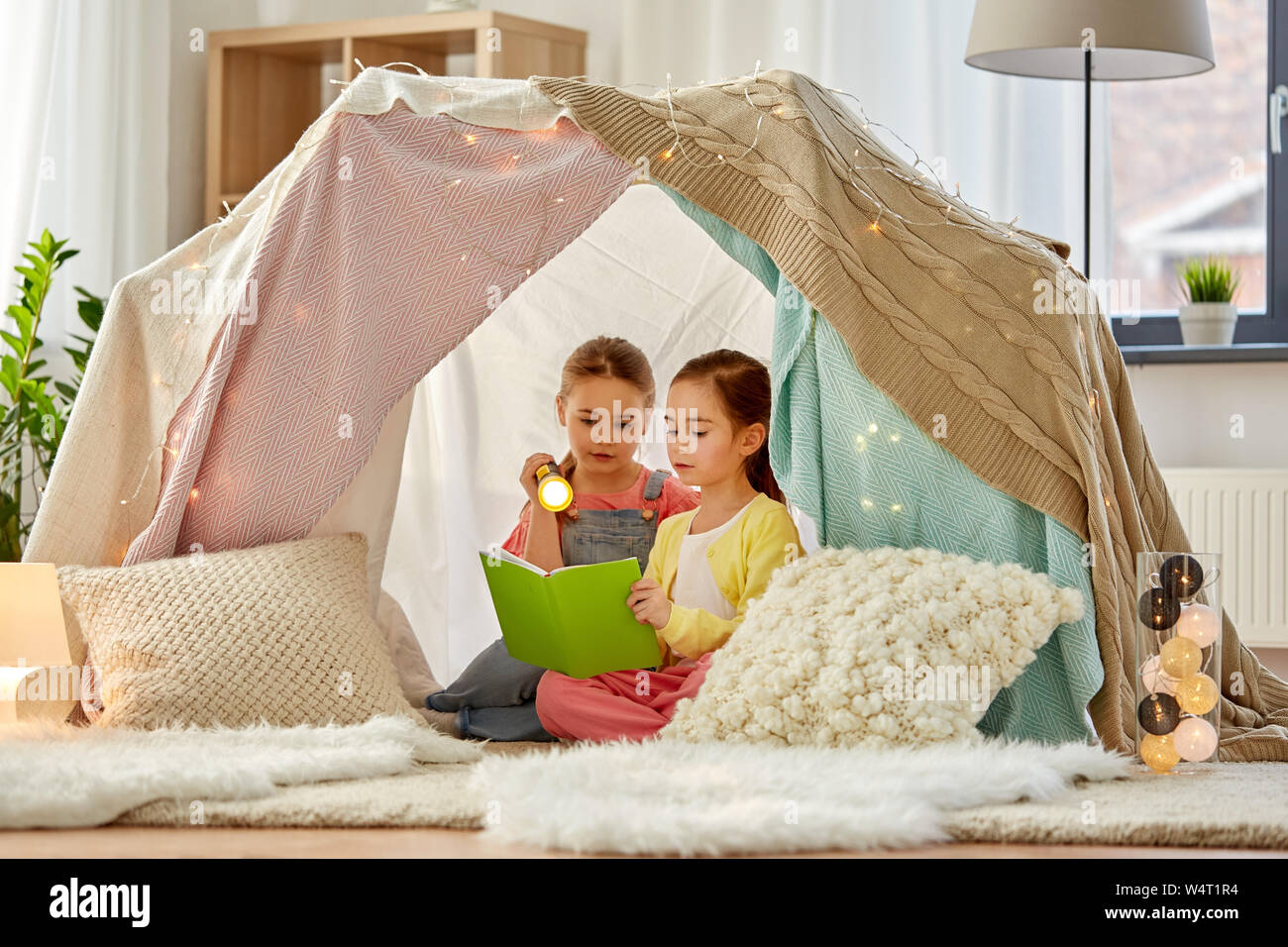 happy girls reading book in kids tent at home Stock Photo - Alamy