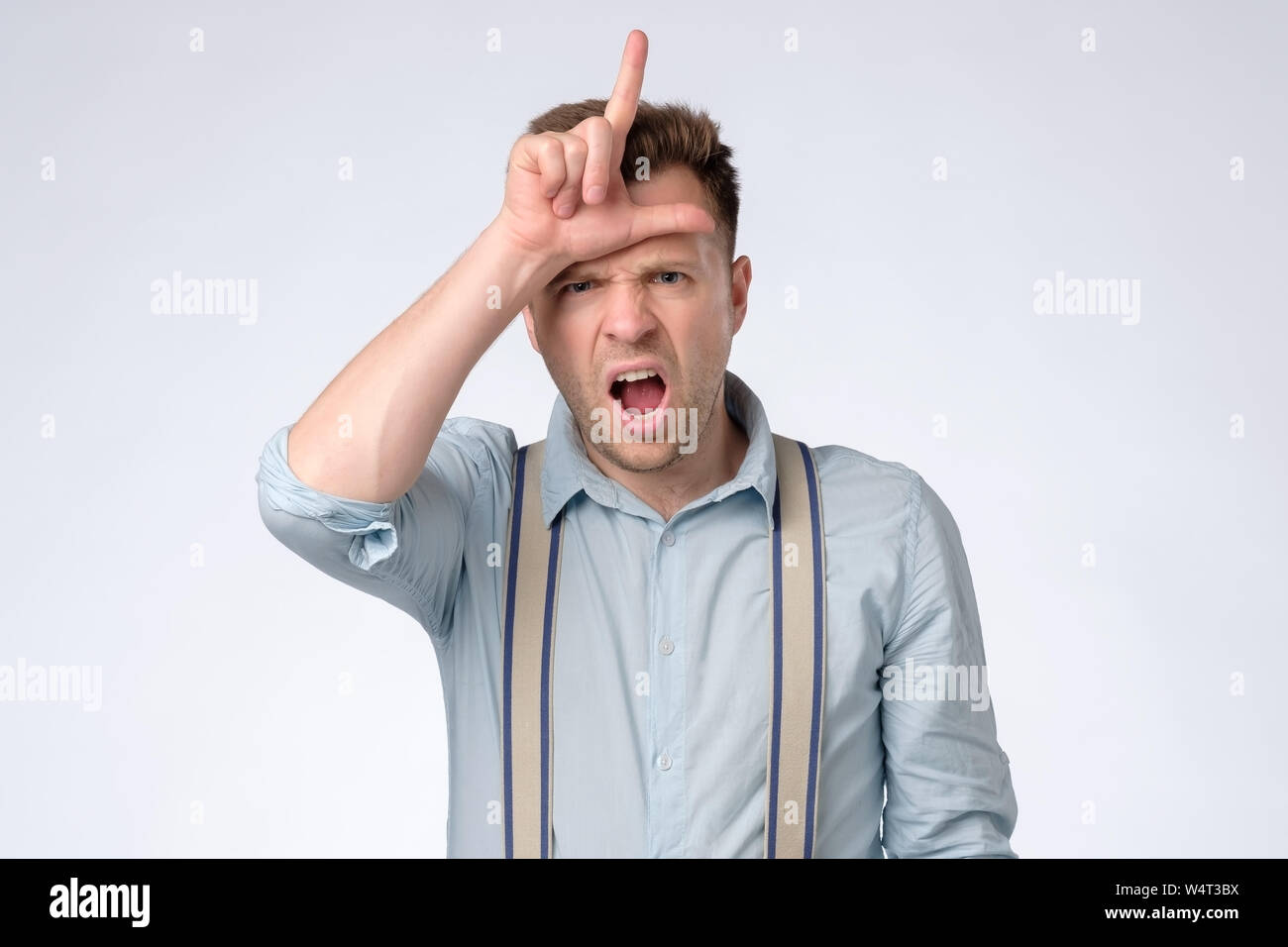 unhappy guy 30s posing on camera and showing loser sign on his forehead ...