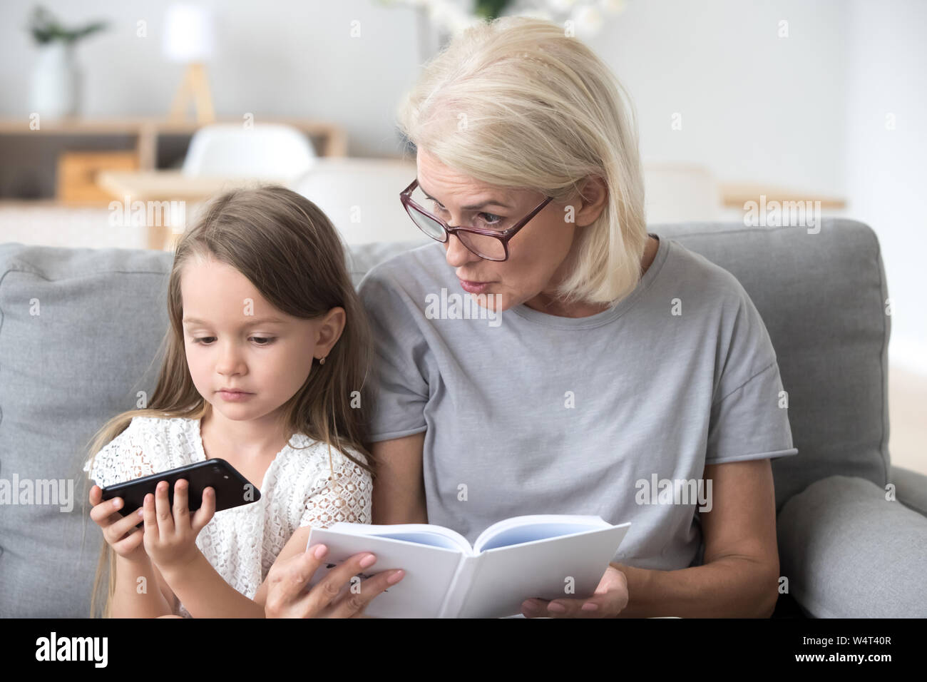 Serious grandma and little granddaughter sitting on couch Stock Photo ...