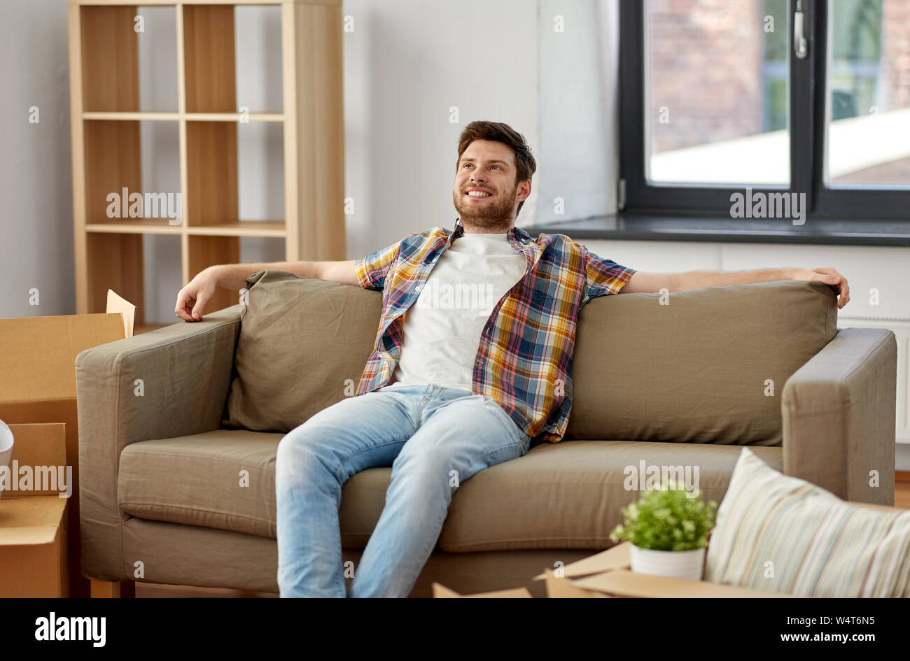 happy man with boxes sitting on sofa at new home Stock Photo - Alamy