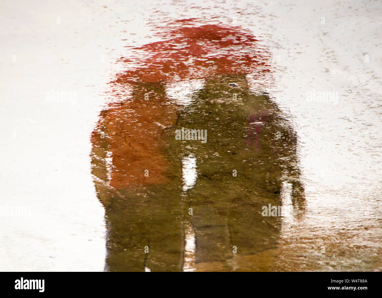 Blurry reflection silhouette in a puddle of couple holding hands while ...