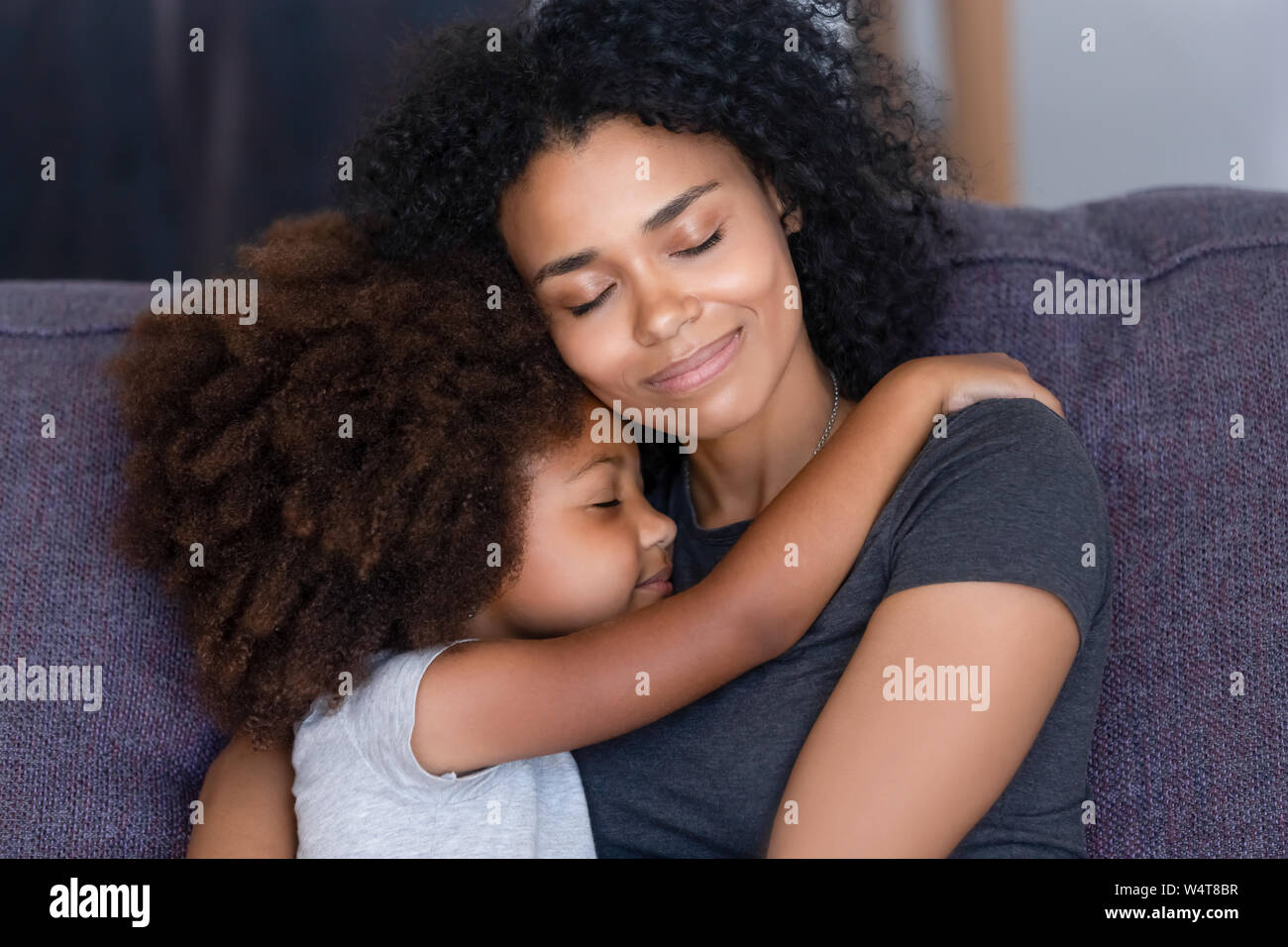 Closeup African Daughter Embracing Mother Sitting On Couch At Home
