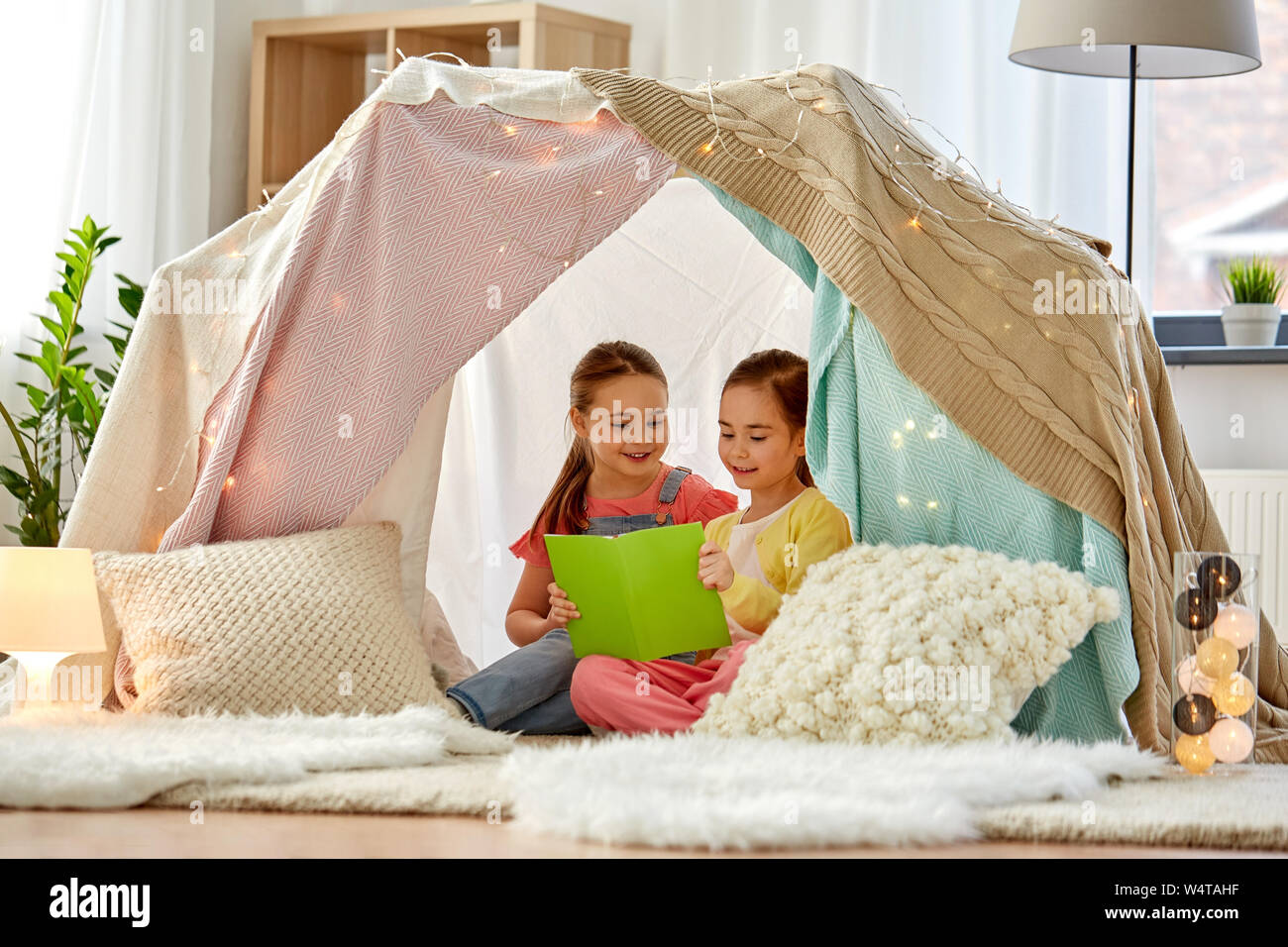 happy girls reading book in kids tent at home Stock Photo - Alamy